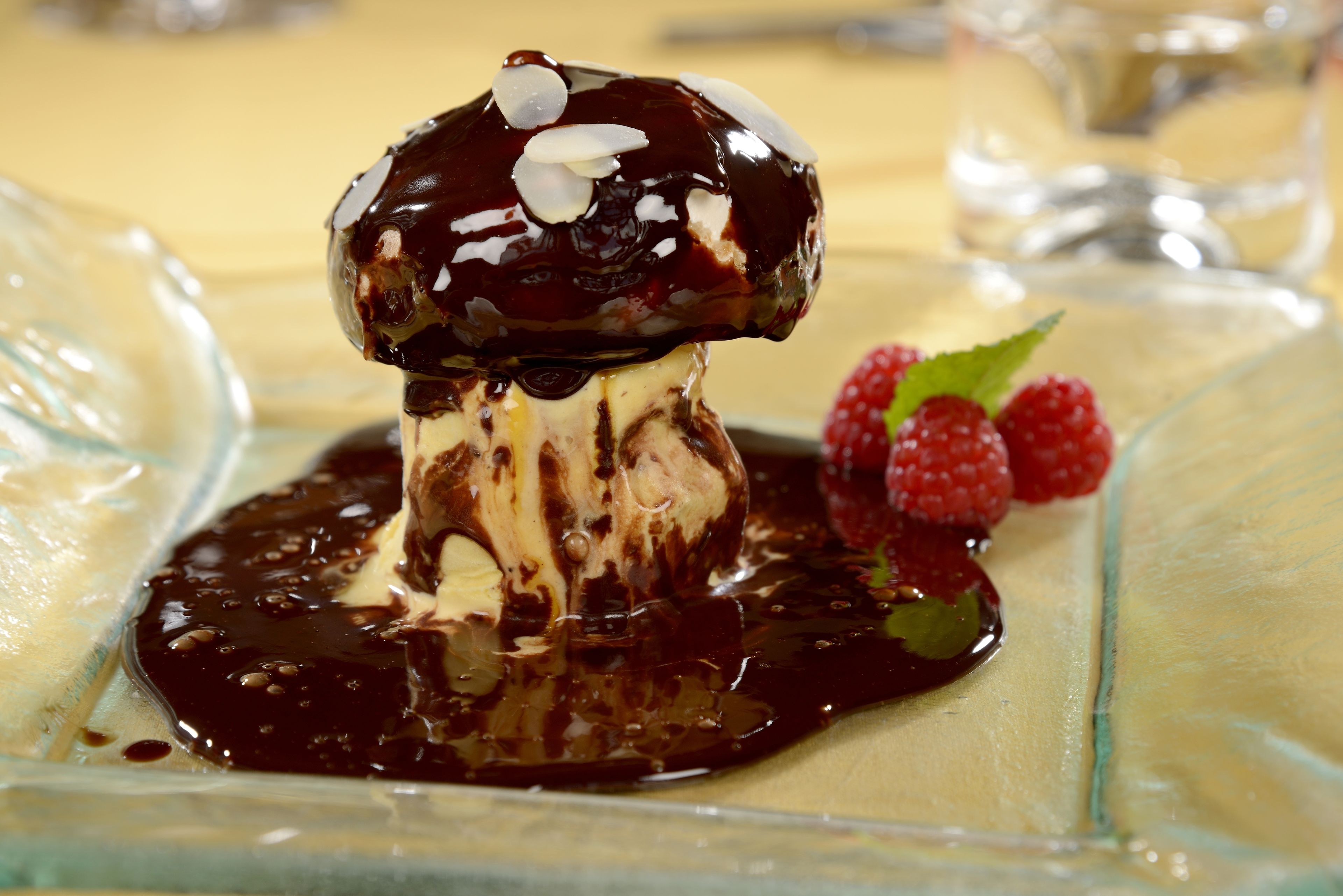 Sobremesa com calda de chocolate e fatias de amêndoa por cima, servida em um prato de vidro.