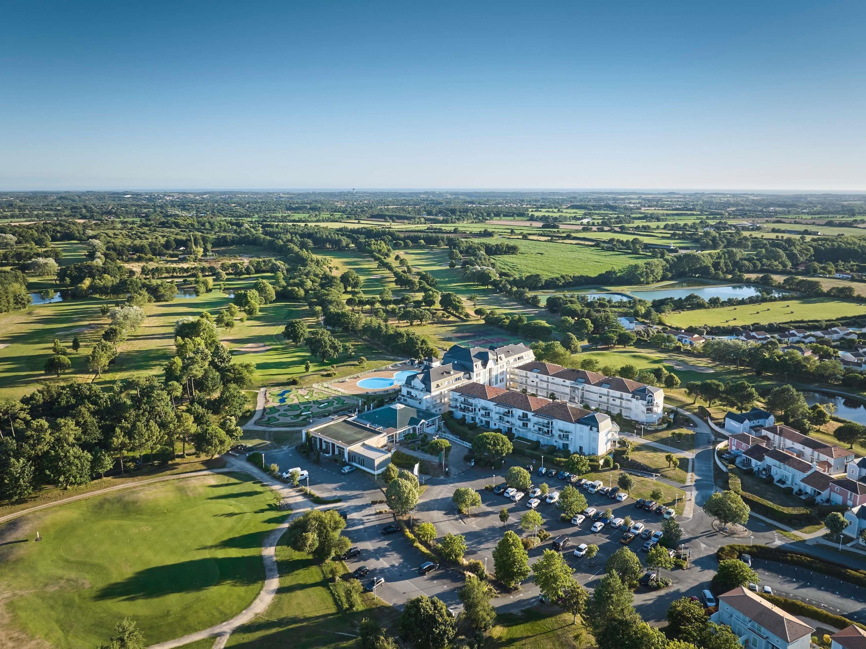 Vista aérea de um campo de golfe com um clube, área de estacionamento e edifícios residenciais.