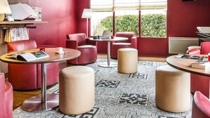 Uma área de estar moderna com assentos de couro vermelho, mesas redondas e um tapete estampado.