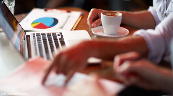 Um laptop, um gráfico circular e uma xícara de café sobre uma mesa.
