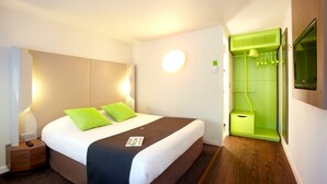 Quarto de hotel com cama, mesa de cabeceira, abajur e um guarda-roupa verde.