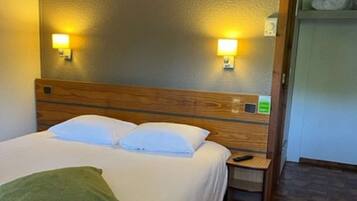 Quarto de hotel com uma cama, duas luminárias de cabeceira, mesa de cabeceira e ar condicionado fixado na parede.