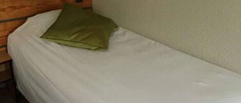 Uma cama de solteiro com cabeceira de madeira, travesseiro verde e luminária branca fixada na parede.