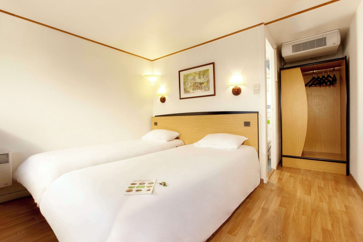 Quarto de hotel com duas camas, cabeceira de madeira, guarda-roupa e um quadro na parede.