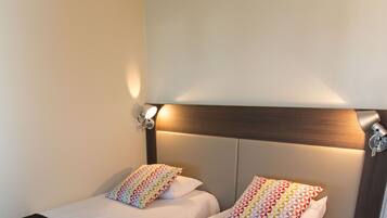 Quarto de hotel com duas camas, cada uma com almofada estampada e cabeceira com iluminação embutida.