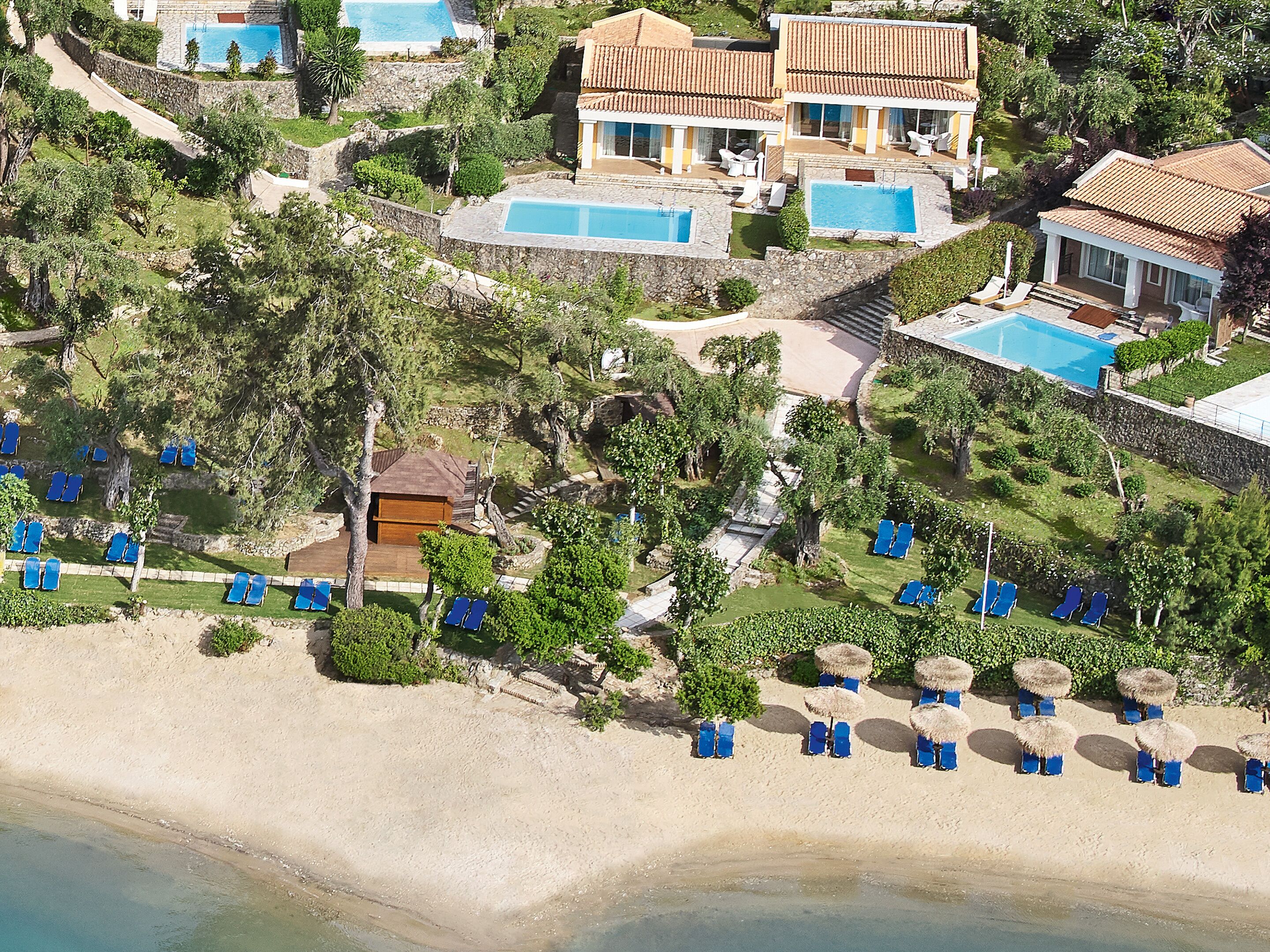 Vista aérea de um resort com várias piscinas, área de praia com espreguiçadeiras e guarda-sóis, e vegetação exuberante.