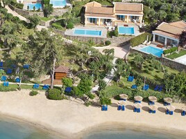 Vista aérea de um resort com várias piscinas, área de praia com espreguiçadeiras e guarda-sóis, e vegetação exuberante.