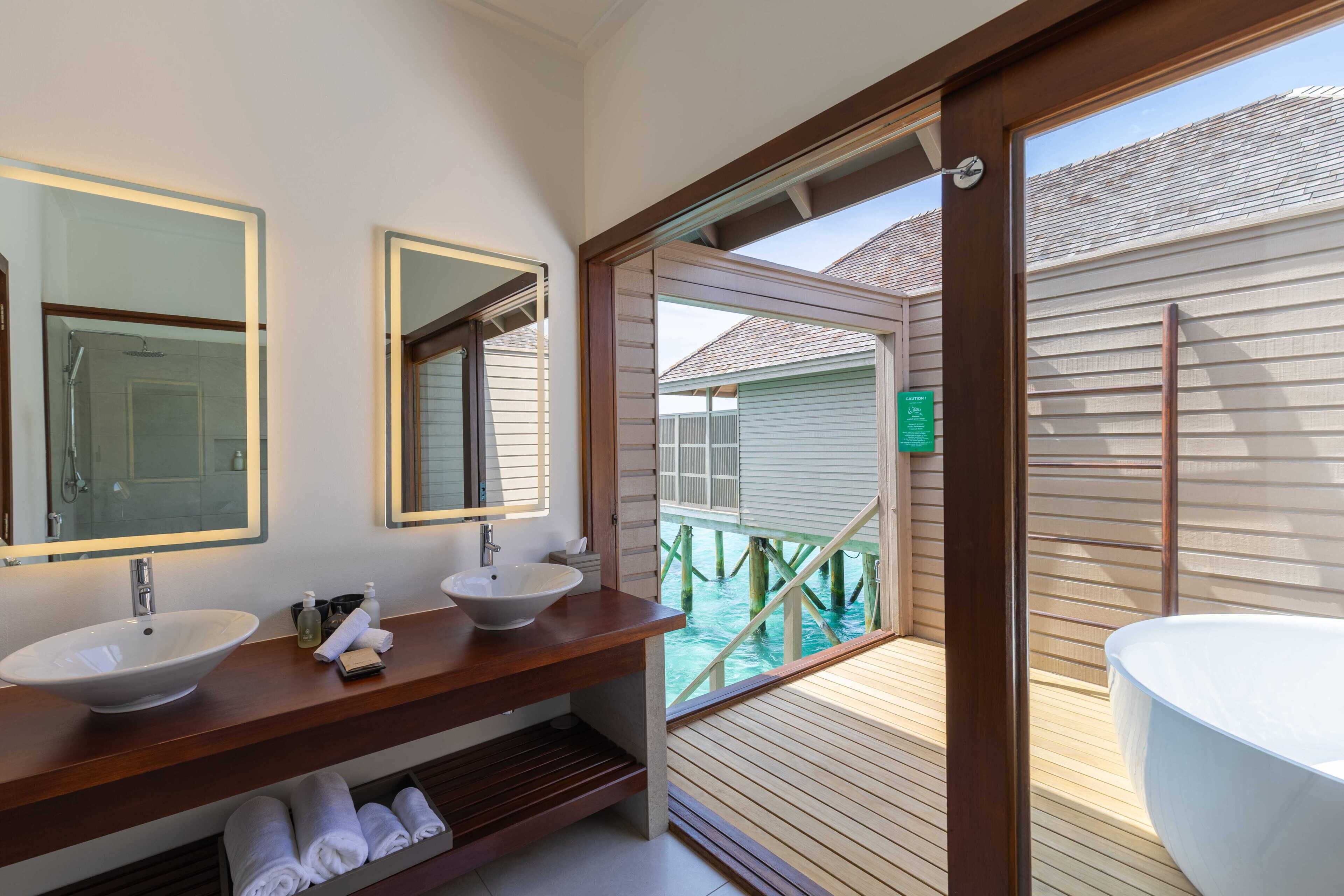 Casa de banho com duas pias, espelho e vista para uma piscina e estrutura sobre a água.