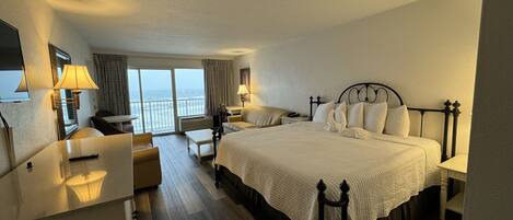 Quarto de hotel com cama grande, uma escrivaninha, uma cadeira e vista para o mar.