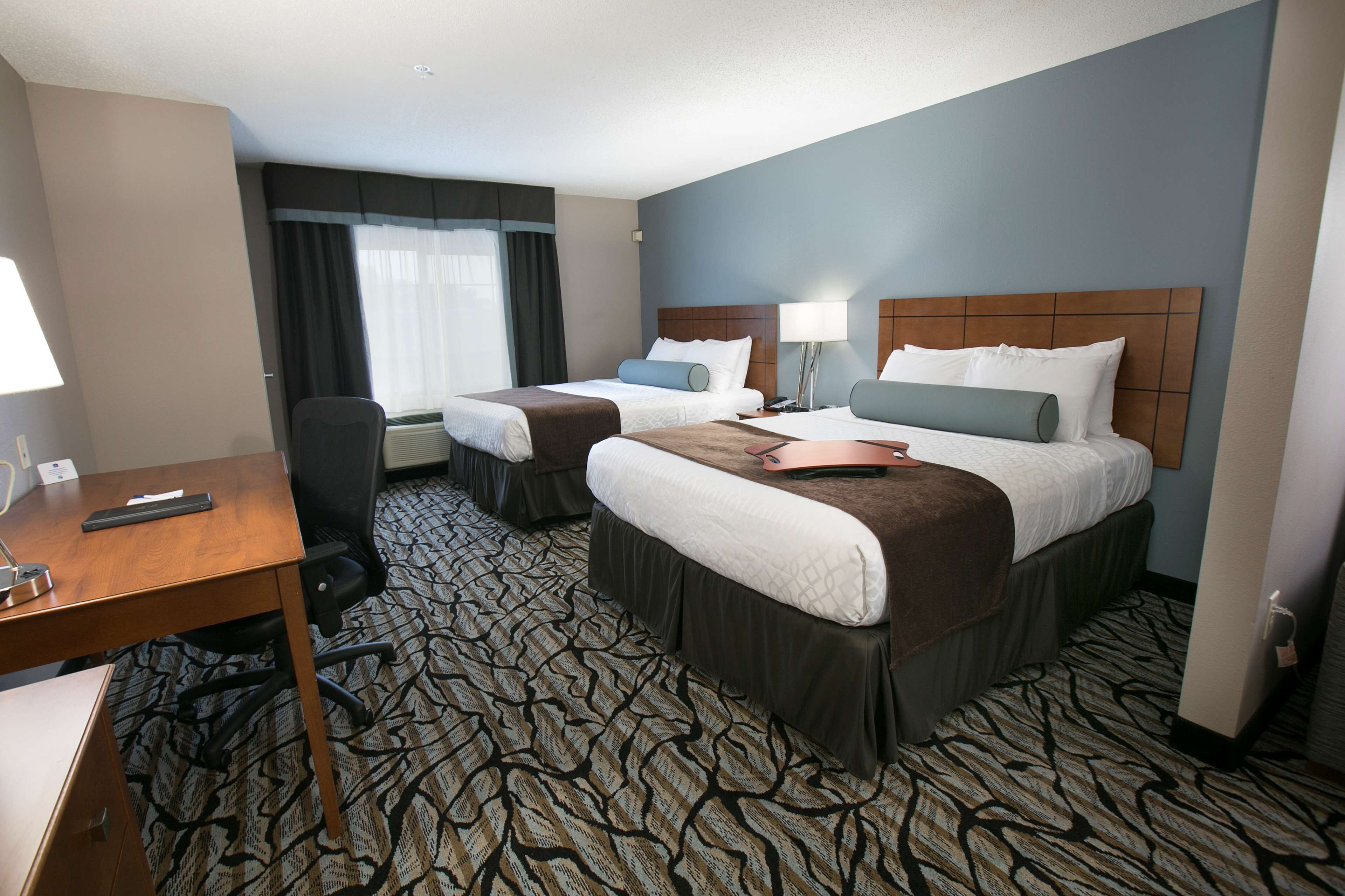 Quarto de hotel com duas camas, uma escrivaninha e uma cadeira.