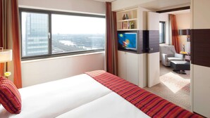 Quarto de hotel com cama, televisão, escrivaninha e vista para a cidade.
