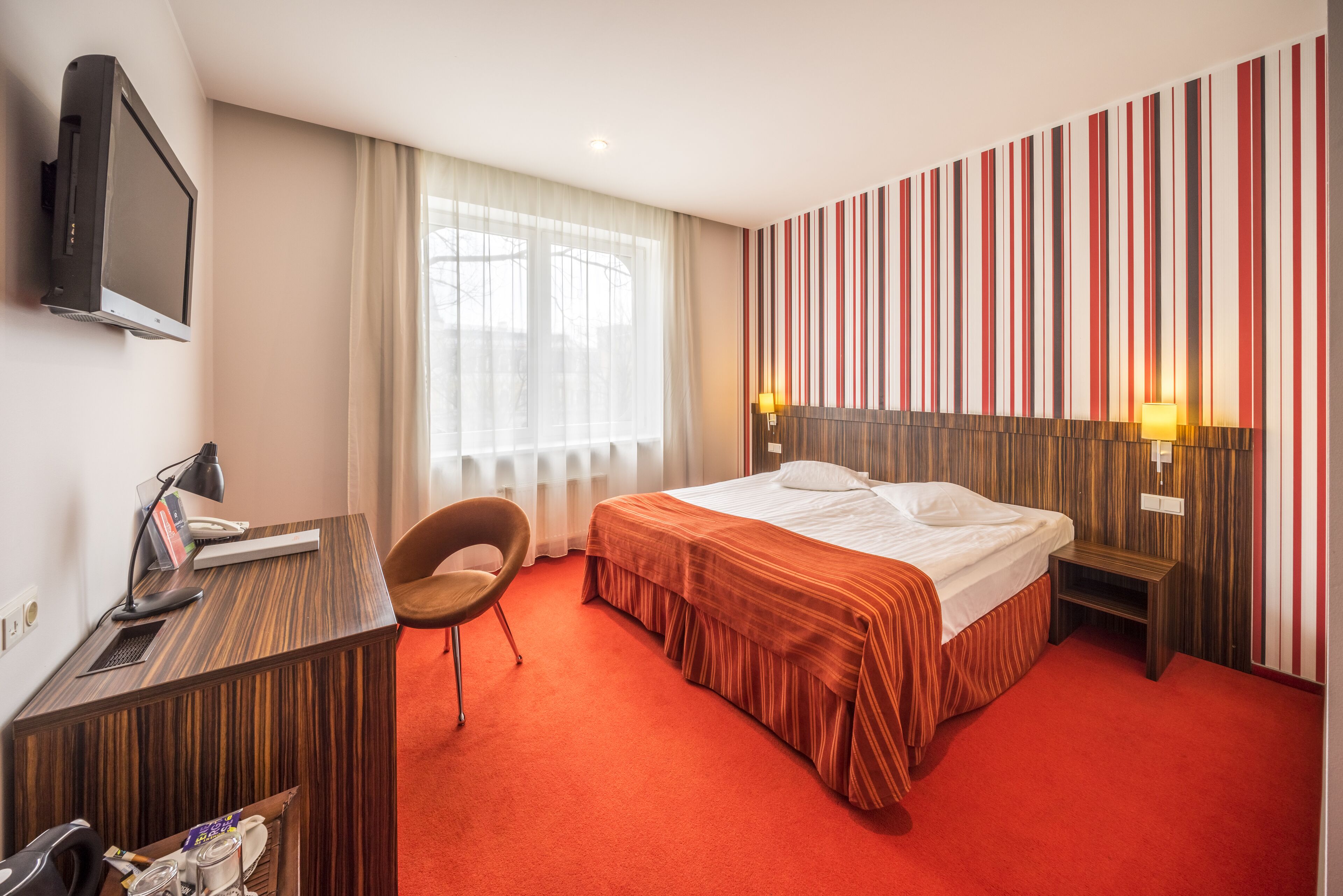 Quarto de hotel com uma cama grande, uma escrivaninha com computador, uma cadeira e uma televisão na parede.