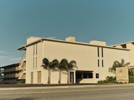 Um edifício moderno com fachada plana, entrada fechada por portão e estacionamento.