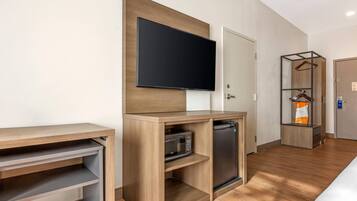 Quarto de hotel moderno com TV de tela plana presa em parede de madeira, micro-ondas embutido e mini-geladeira.