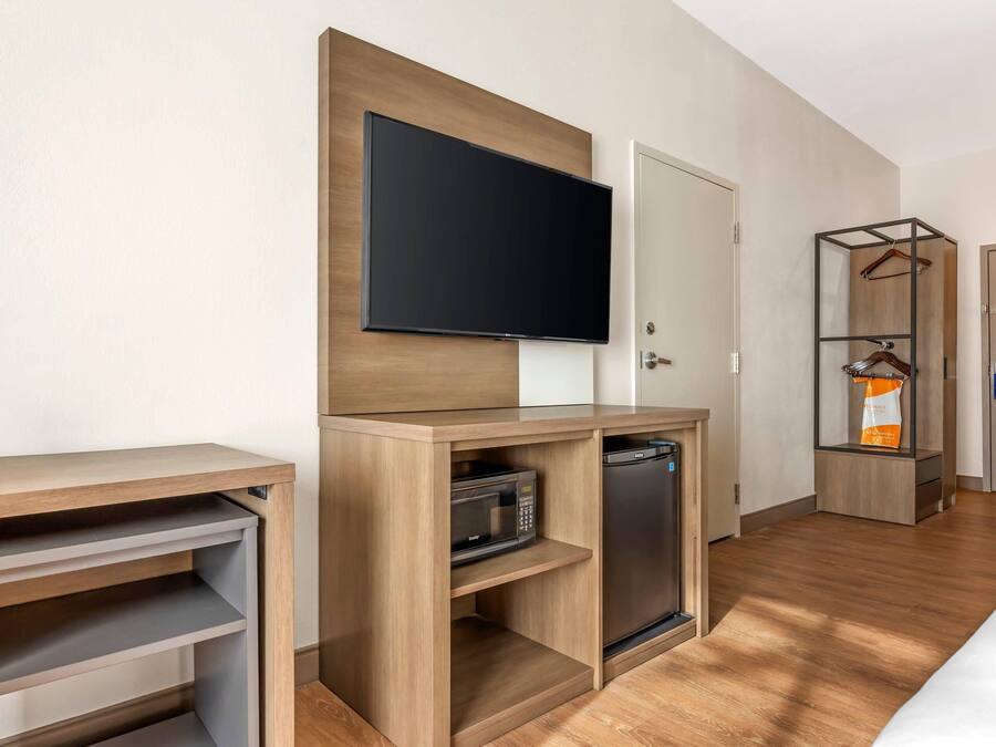 Quarto de hotel moderno com TV de tela plana presa em parede de madeira, micro-ondas embutido e mini-geladeira.