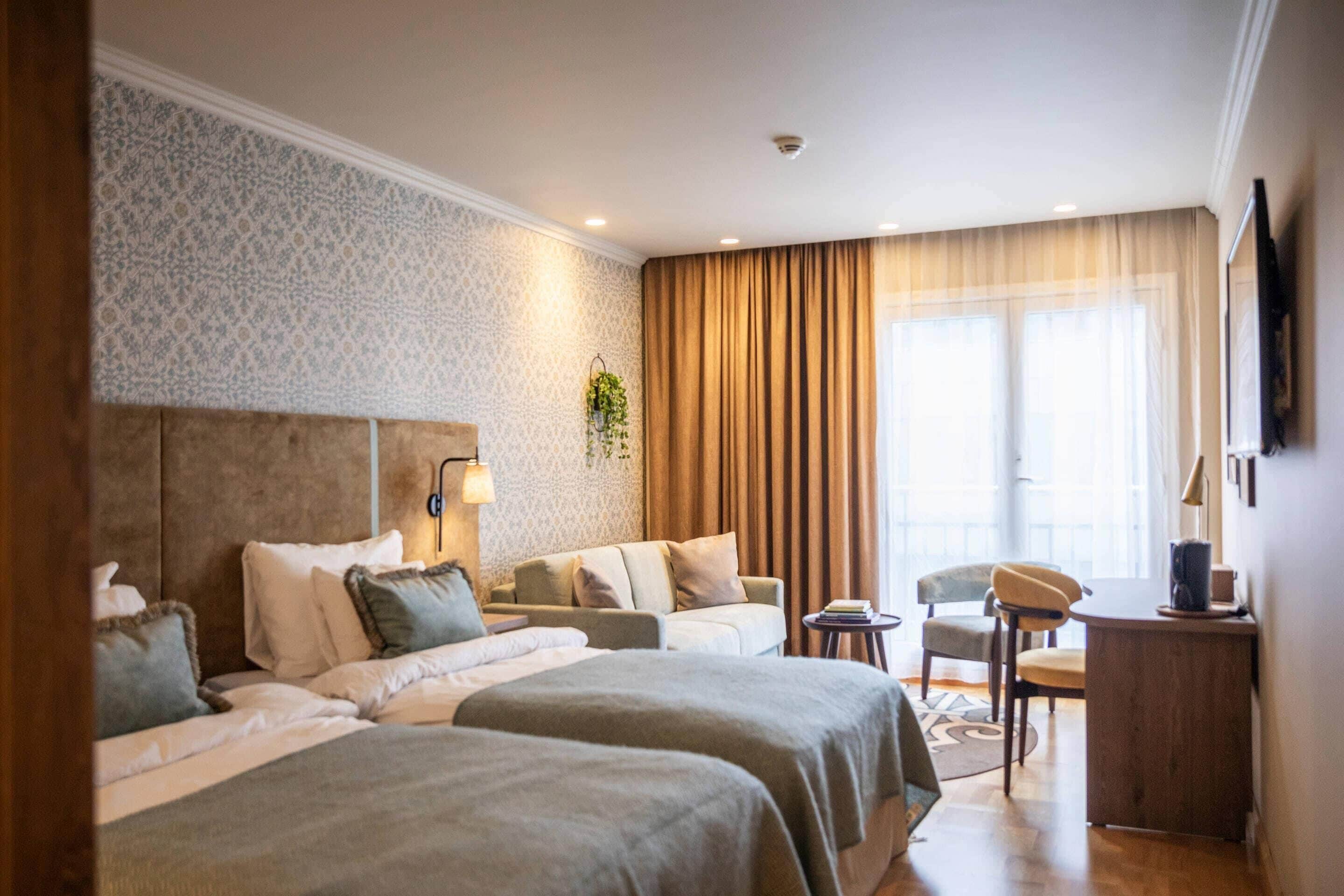 Quarto de hotel com duas camas, um sofá, uma escrivaninha e uma televisão.