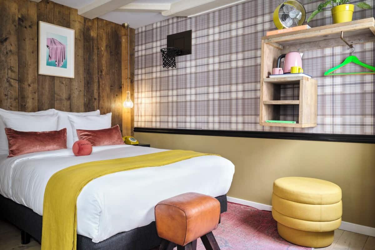 Quarto com cama, parede de madeira, prateleira com objetos e planta pendente.