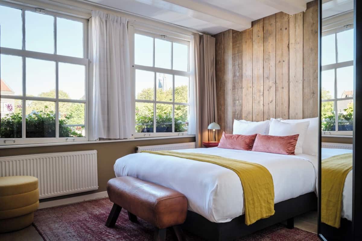 Quarto com cama grande, parede de madeira e janela com cortinas.