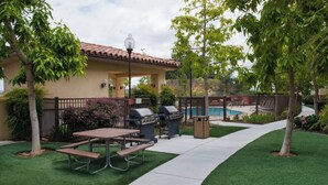 Área de pátio com mesa para piquenique, churrasqueira e vista para a piscina.