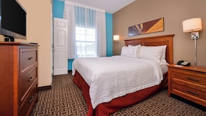 Quarto de hotel com cama, televisão, escrivaninha e abajur.