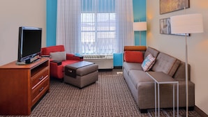 Quarto de hotel com televisão, sofá vermelho e cinzento, uma pequena mesa e uma luminária.