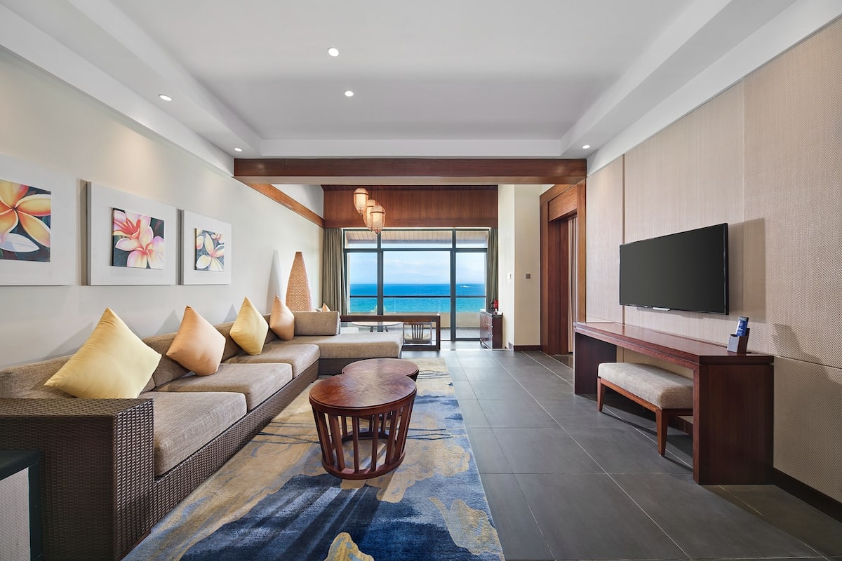 Uma sala de estar moderna com sofá, mesa de centro e televisão, com vista para o oceano.