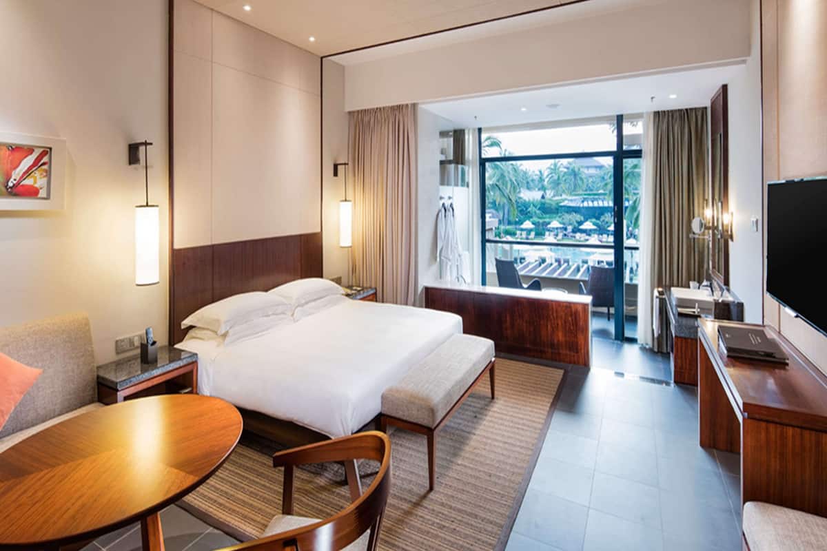 Quarto de hotel com cama grande, escrivaninha, cadeira, televisão e vista para o exterior.