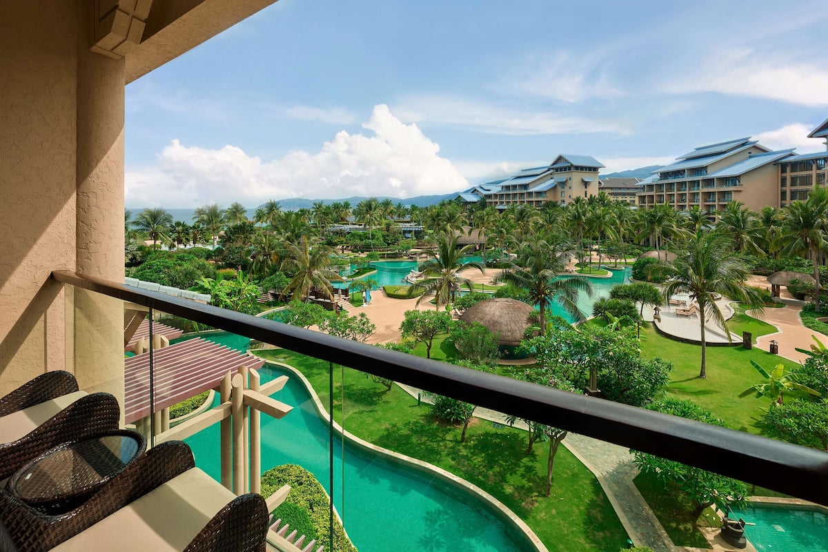 Um resort com piscina, palmeiras e vista para o oceano.