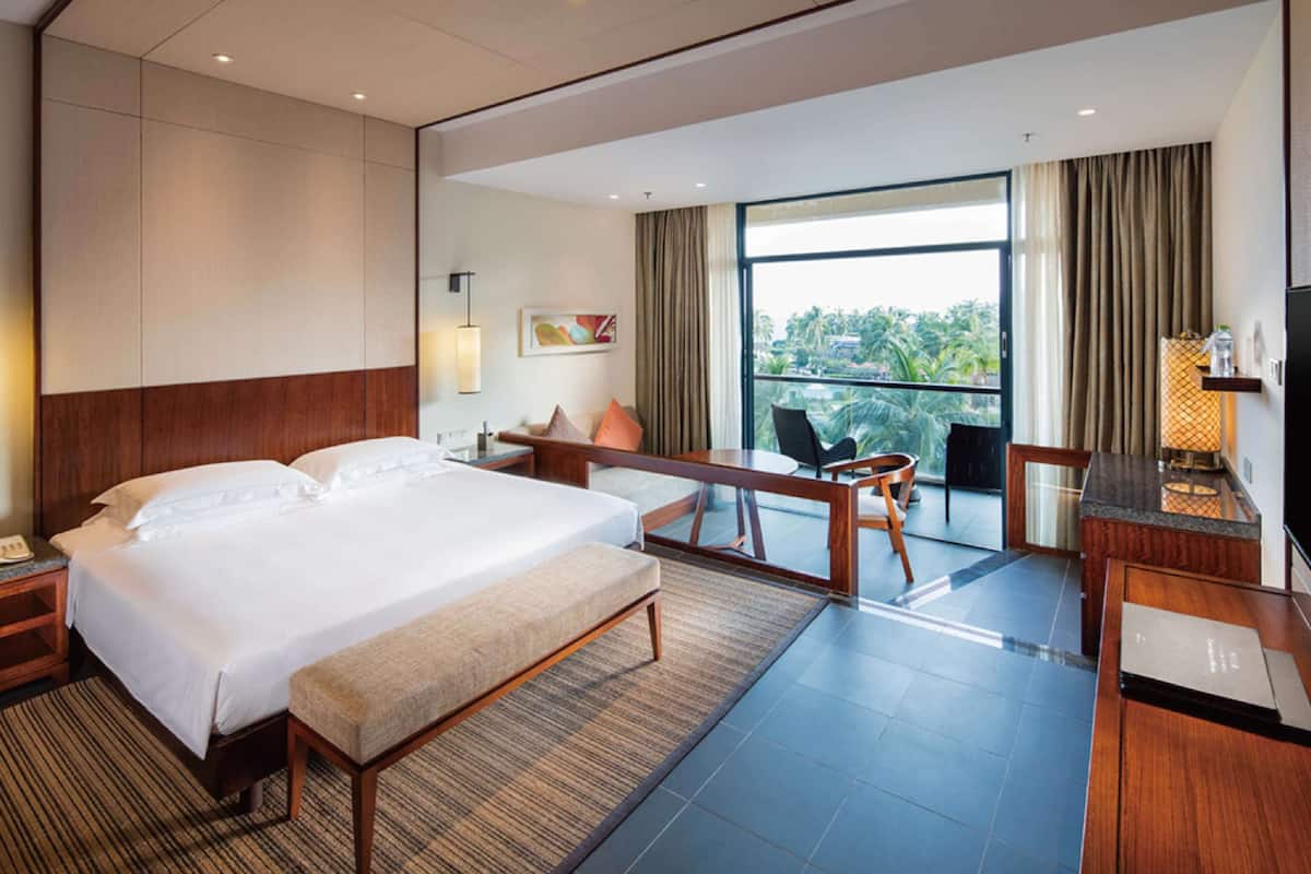 Quarto de hotel com uma cama grande, uma escrivaninha, uma cadeira e vista para o exterior.