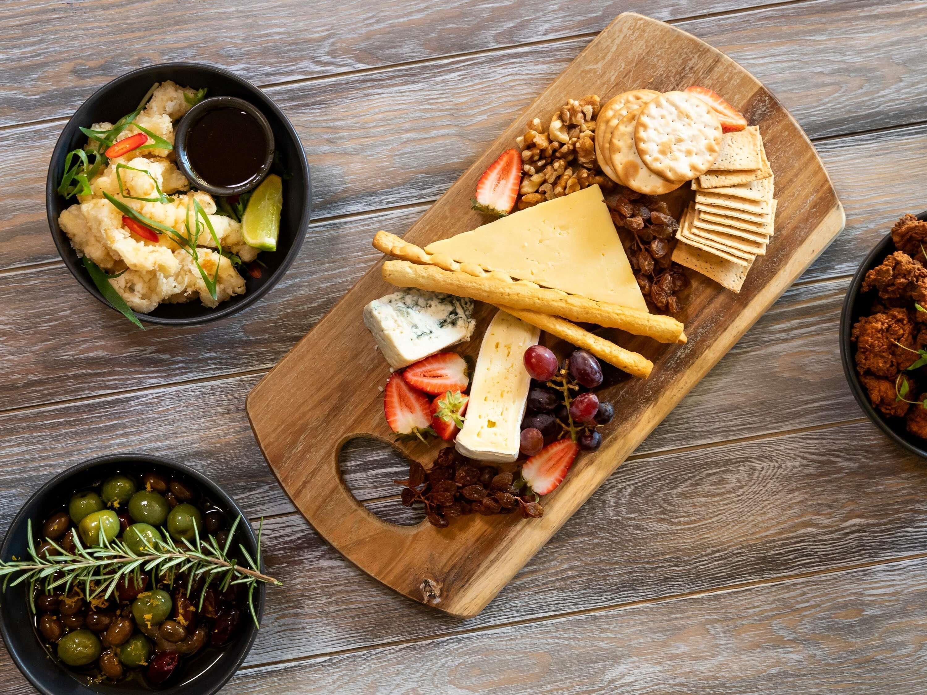 Tábua de madeira com queijo, bolachas, uvas e frutos secos.