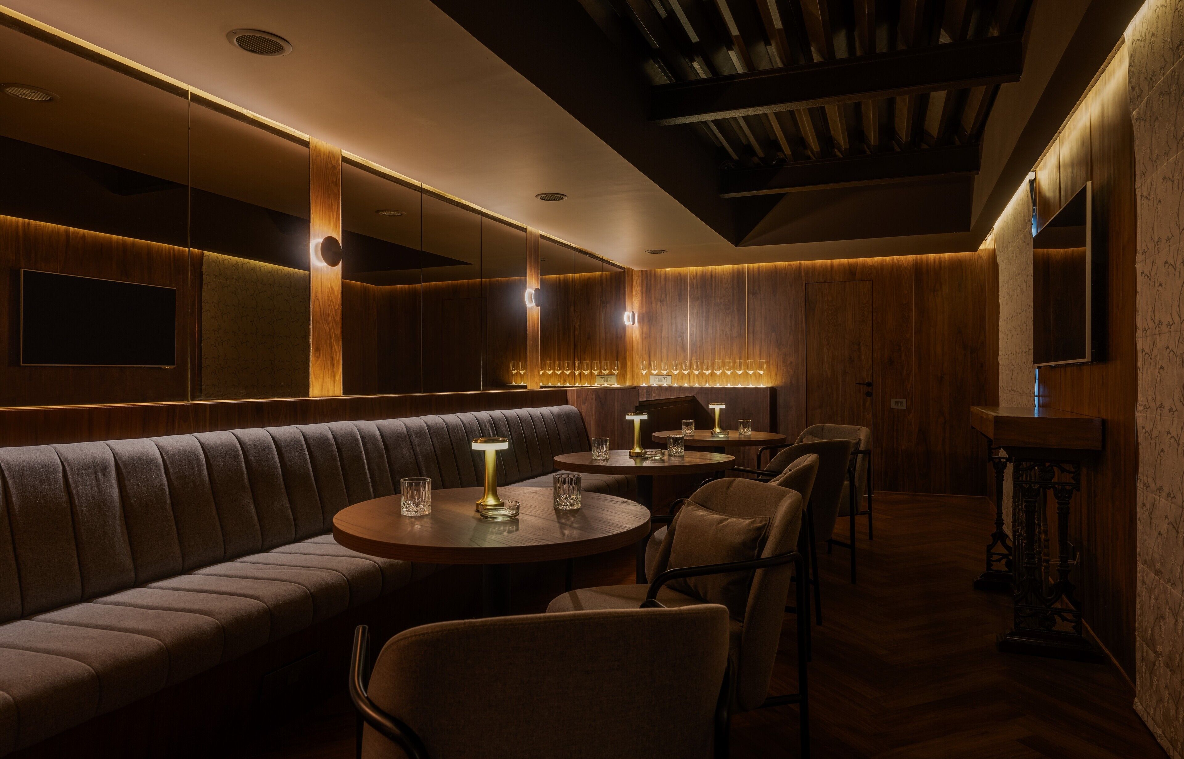 Um restaurante com iluminação suave, painéis de madeira, um longo banco, mesas redondas e cadeiras.