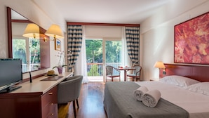Quarto de hotel com cama, escrivaninha, cadeira e varanda com cortinas.