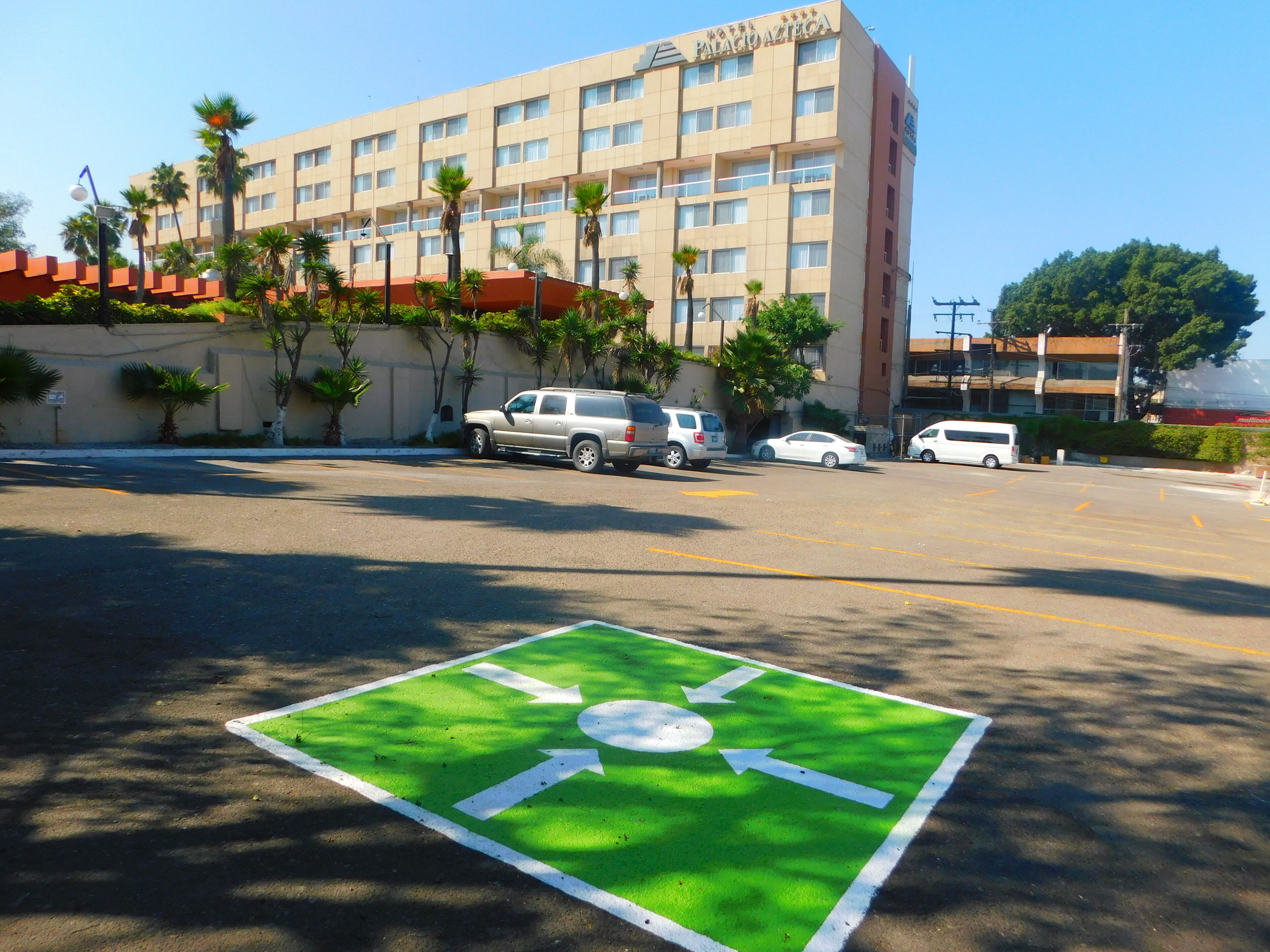 Hotel com estacionamento, caminhos para pedestres demarcados e palmeiras.