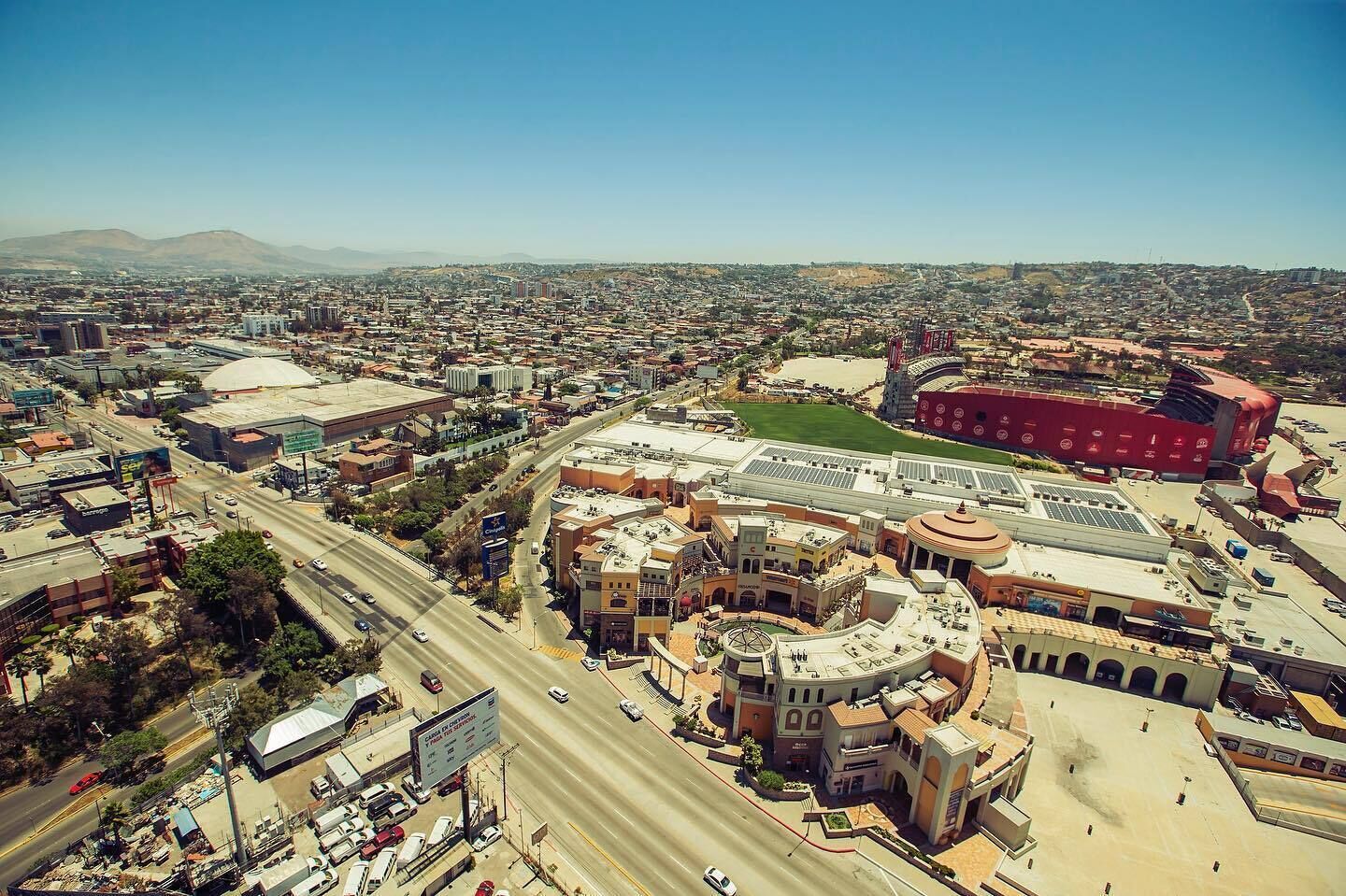 Vista aérea de um horizonte urbano com um estádio em destaque, ruas largas e edifícios ao redor.