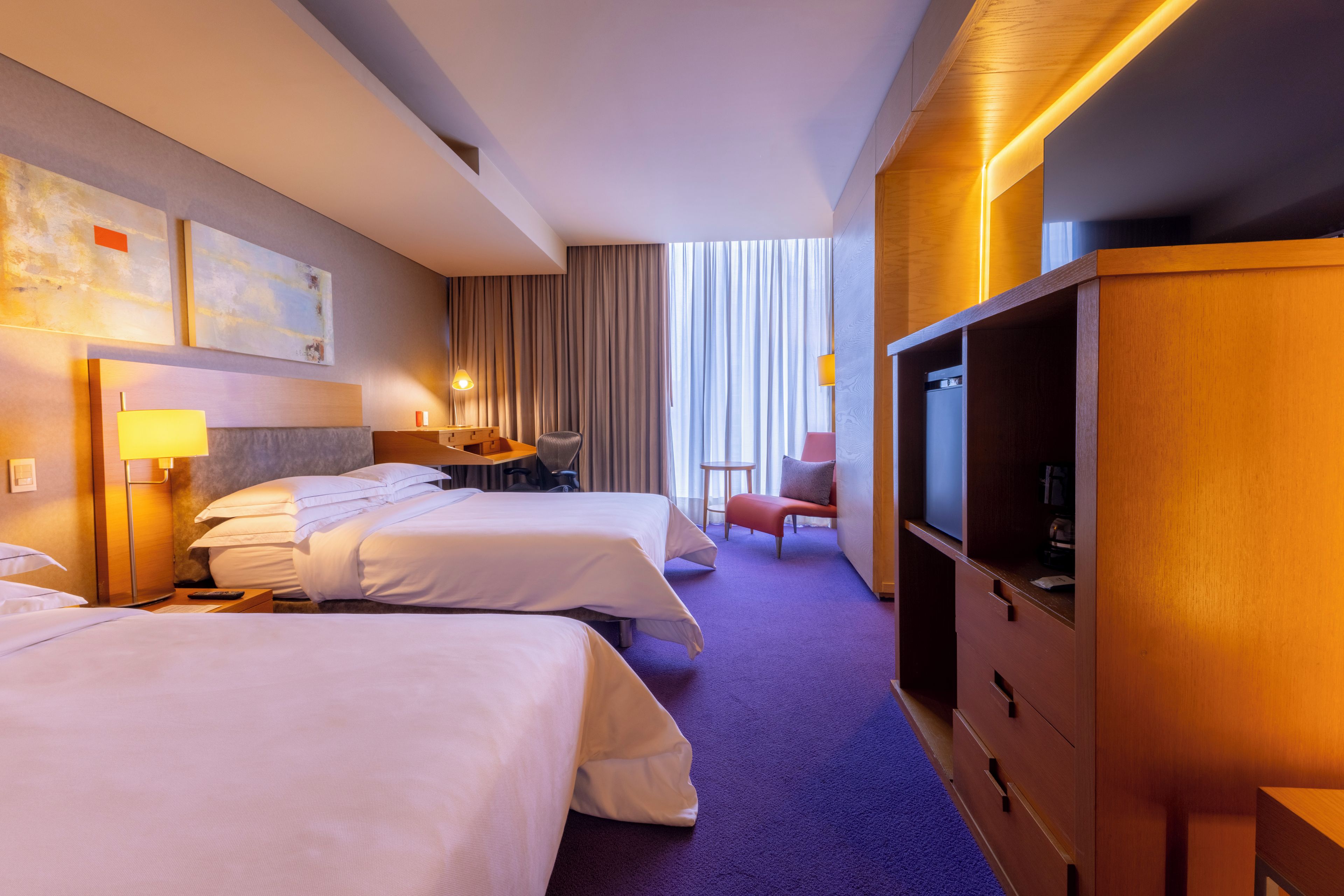 Quarto de hotel com duas camas, televisão, escrivaninha e uma cadeira.