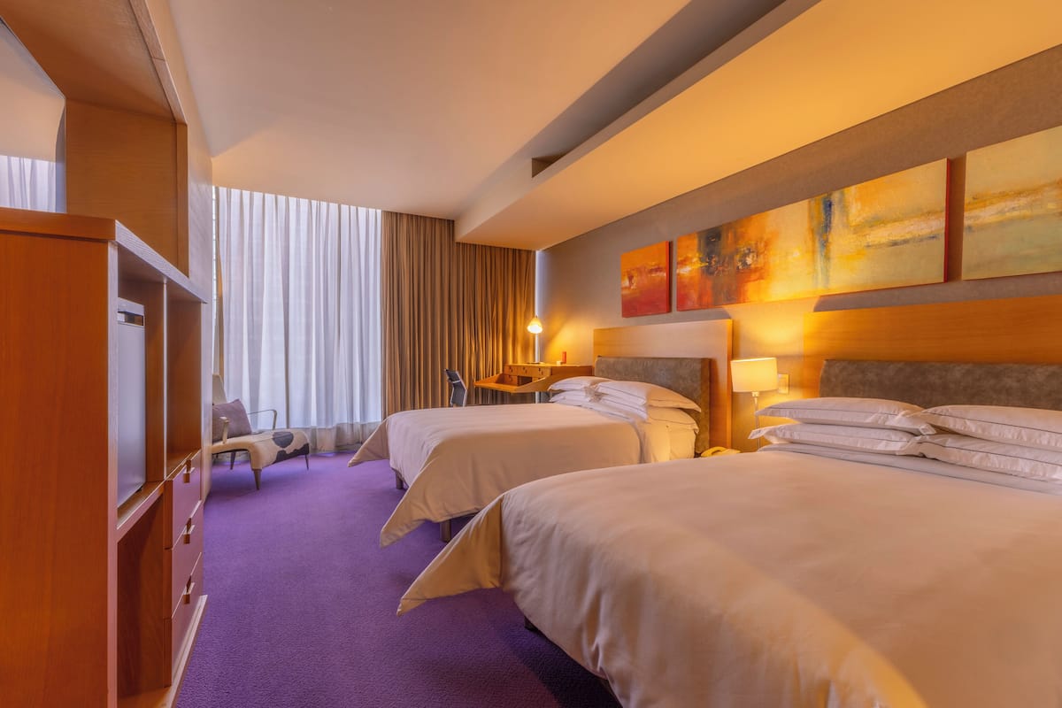 Quarto de hotel com duas camas, uma escrivaninha, uma cadeira e um guarda-roupa.