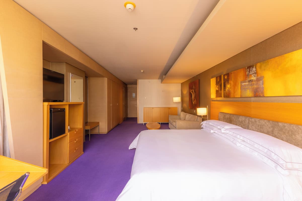 Quarto de hotel com cama, escrivaninha, guarda-roupa, área de estar e um quadro na parede.