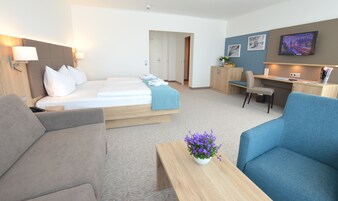 Quarto de hotel com cama, escrivaninha, cadeira e sofá.
