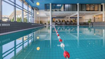 Piscina interior com água cristalina, bloco de partida com boias demarcando as pistas e área de recepção com assentos e balcão.