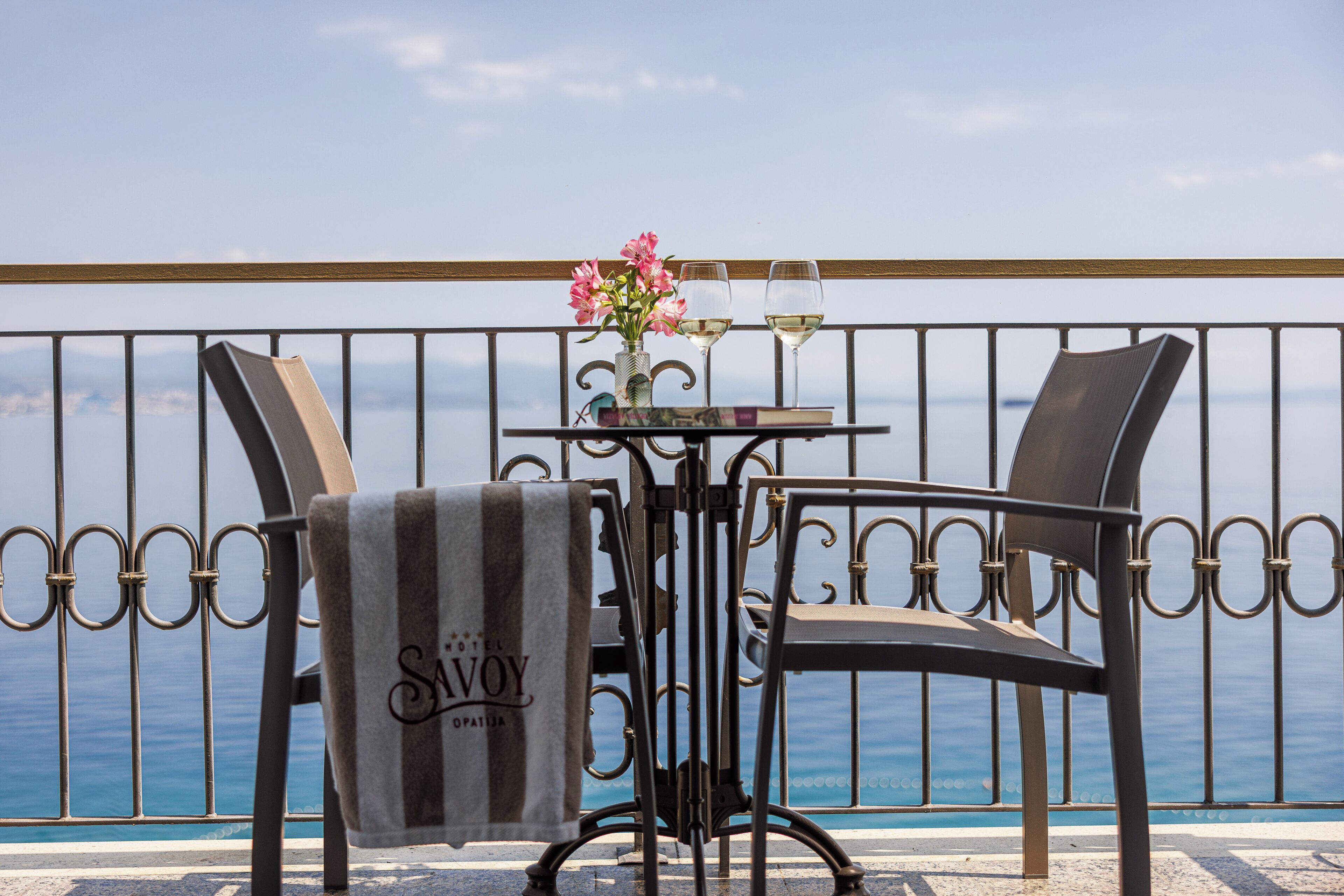 Mesa com duas cadeiras, um vaso com flores e dois copos de vinho branco, com vista para a água.
