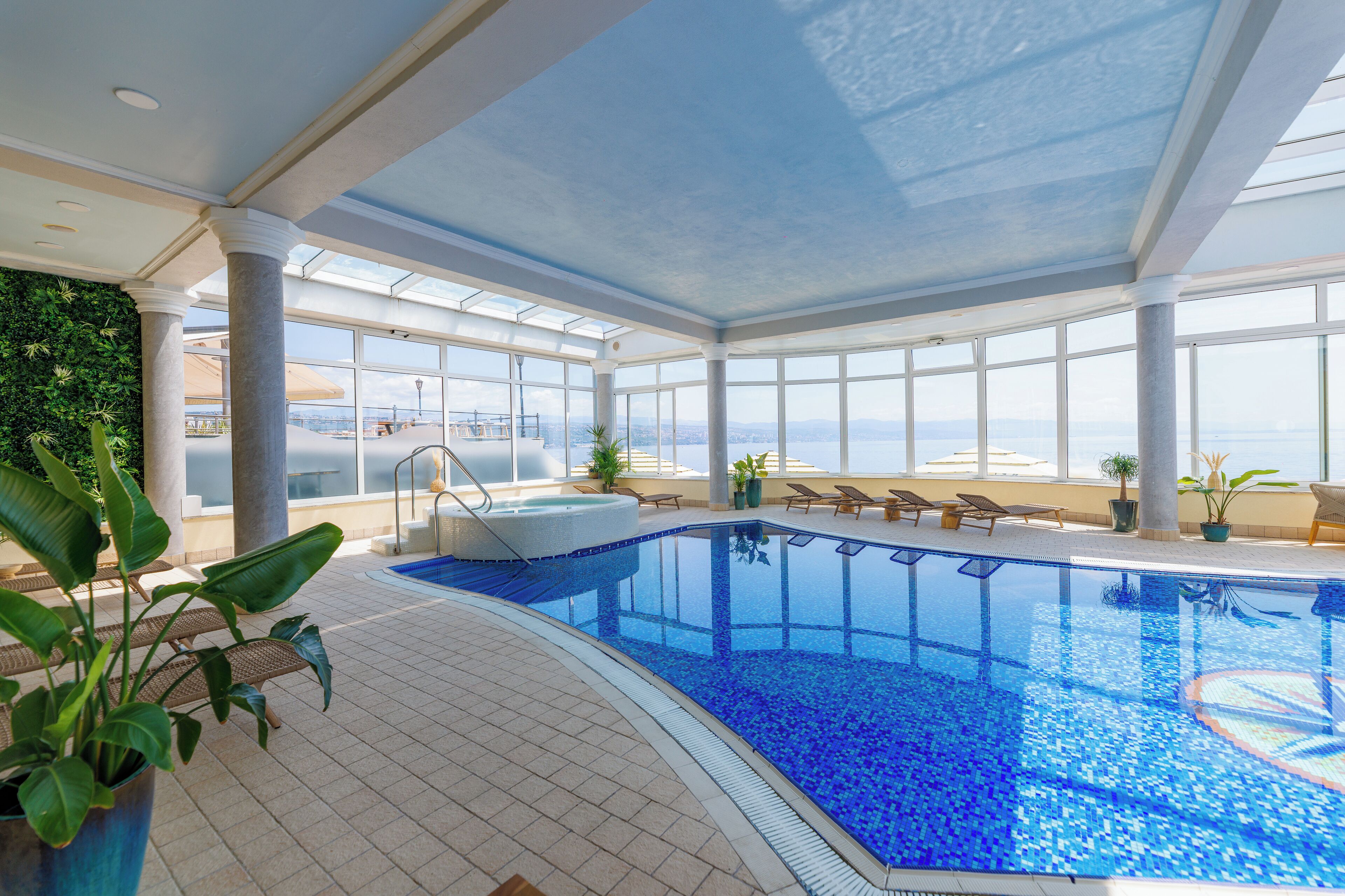 Piscina interna com paredes de vidro transparente, hidromassagem e espreguiçadeiras.