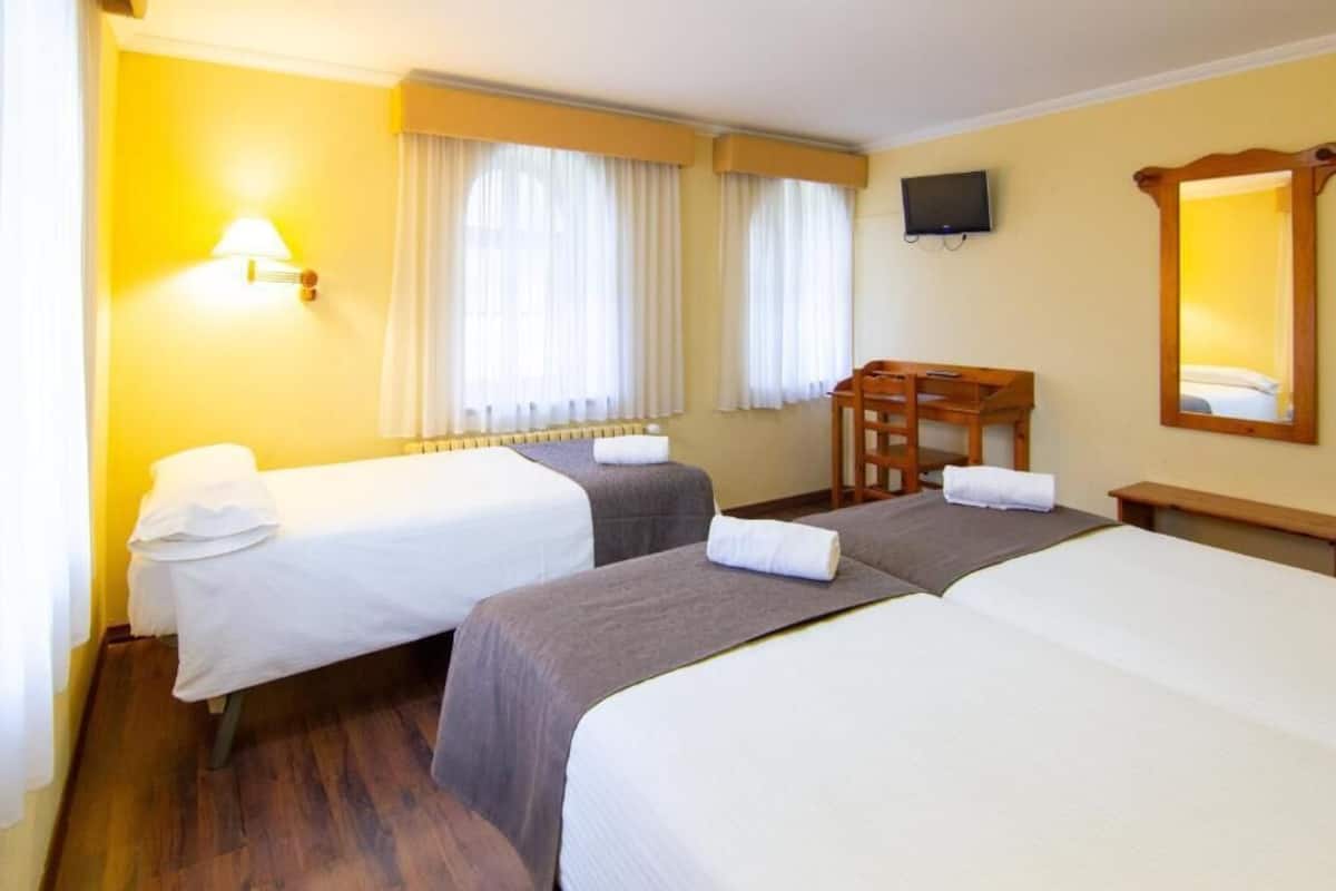 Quarto de hotel com duas camas, uma escrivaninha, uma cadeira, uma televisão e um espelho.