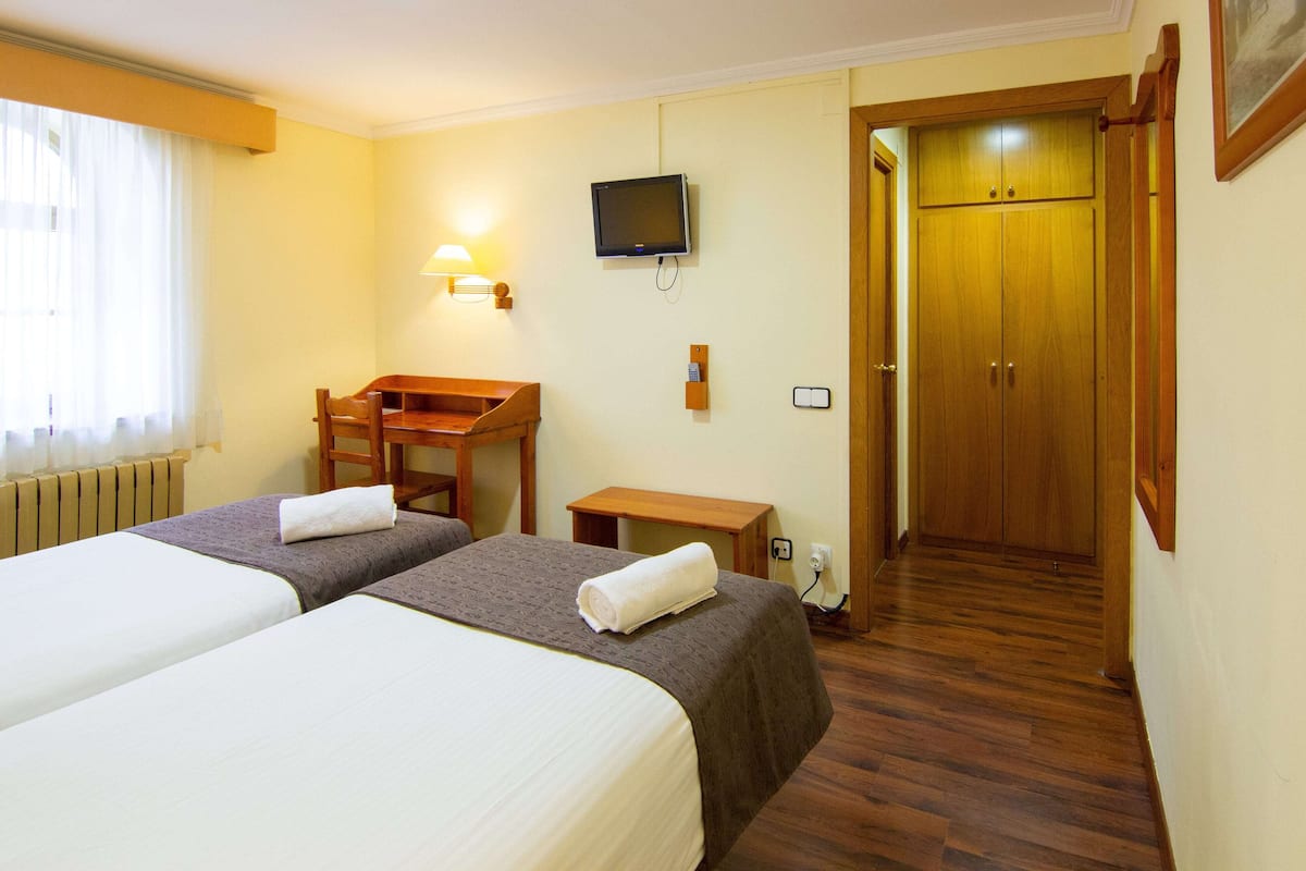 Quarto de hotel com duas camas, uma mesa, uma televisão e um guarda-roupa.