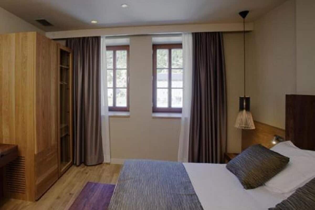 Quarto com cama, guarda-roupa de madeira, janela com cortinas e luminária de cabeceira.