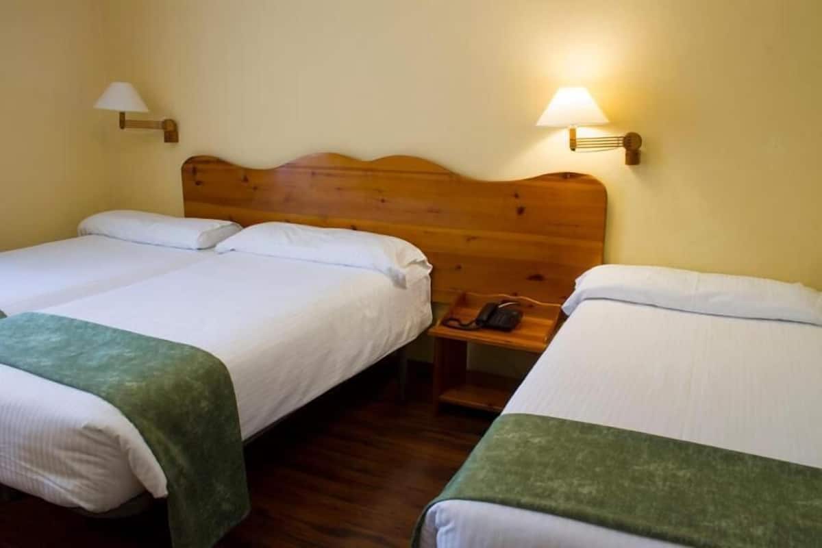 Quarto de hotel com duas camas de solteiro, cabeceiras de madeira, abajures e um telefone em uma mesinha de cabeceira.
