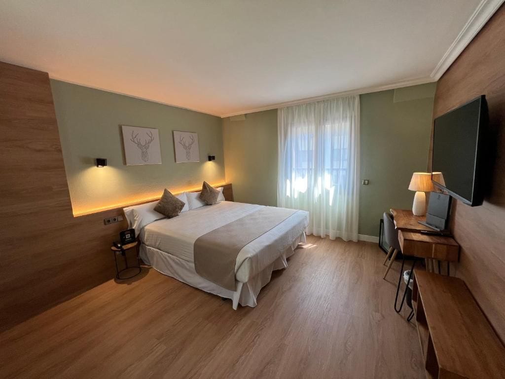 Quarto de hotel moderno com uma cama grande, mesas de cabeceira, uma escrivaninha com abajur e televisão de tela plana.
