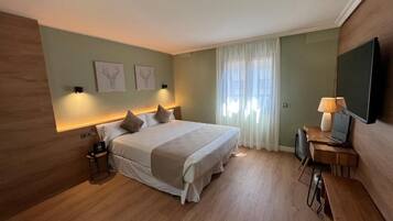 Quarto de hotel moderno com uma cama grande, mesas de cabeceira, uma escrivaninha com abajur e televisão de tela plana.