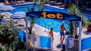 Uma área de piscina com sinalização de hidromassagem, espreguiçadeiras e guarda-sóis.