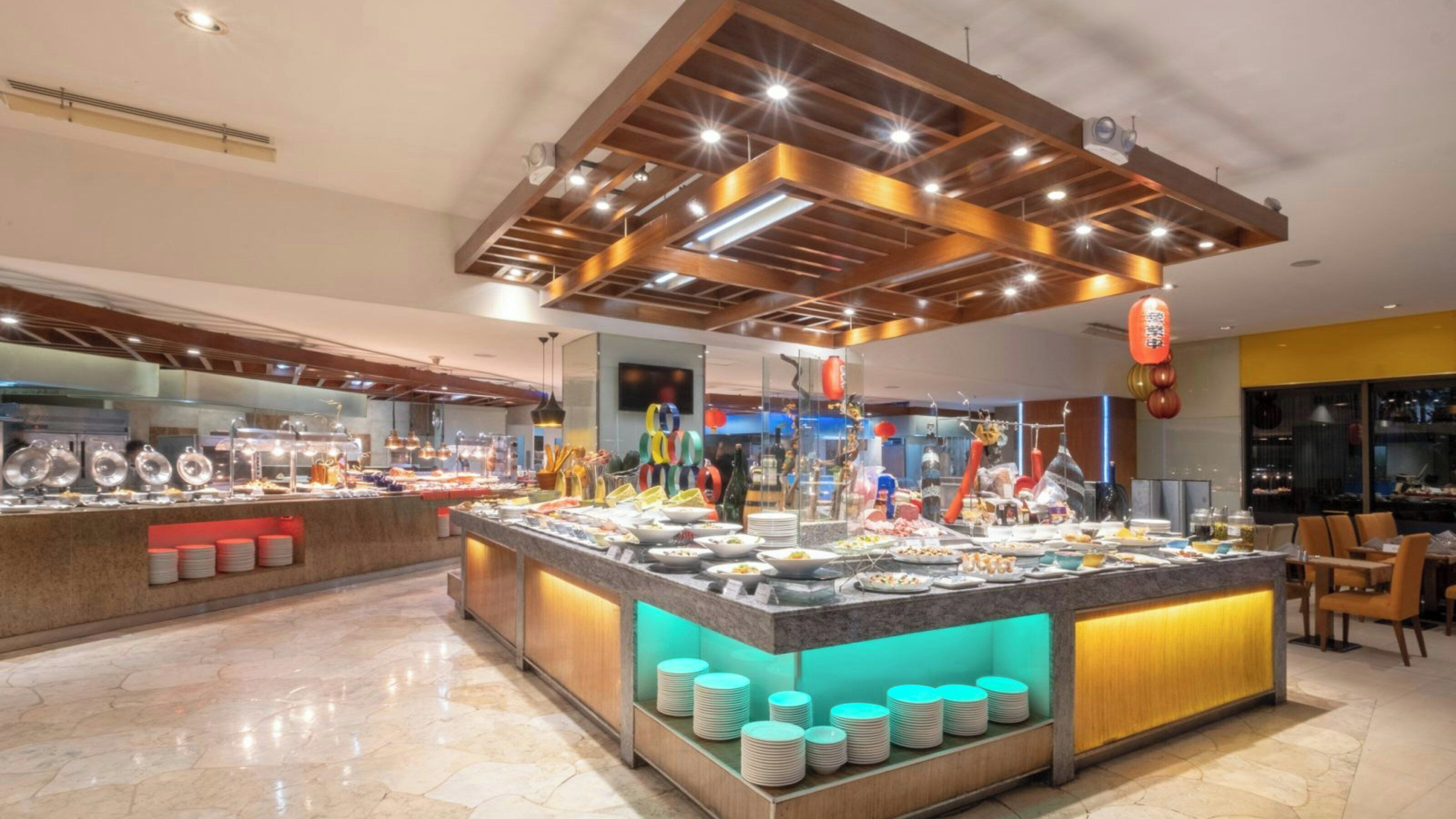 Uma área de buffet com diversas estações de comida, um balcão de serviço central e disposição de mesas.