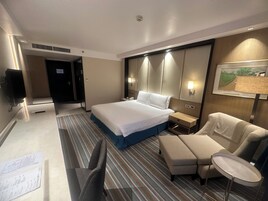 Quarto de hotel com uma cama grande, uma escrivaninha com cadeira, uma mesinha e um sofá.
